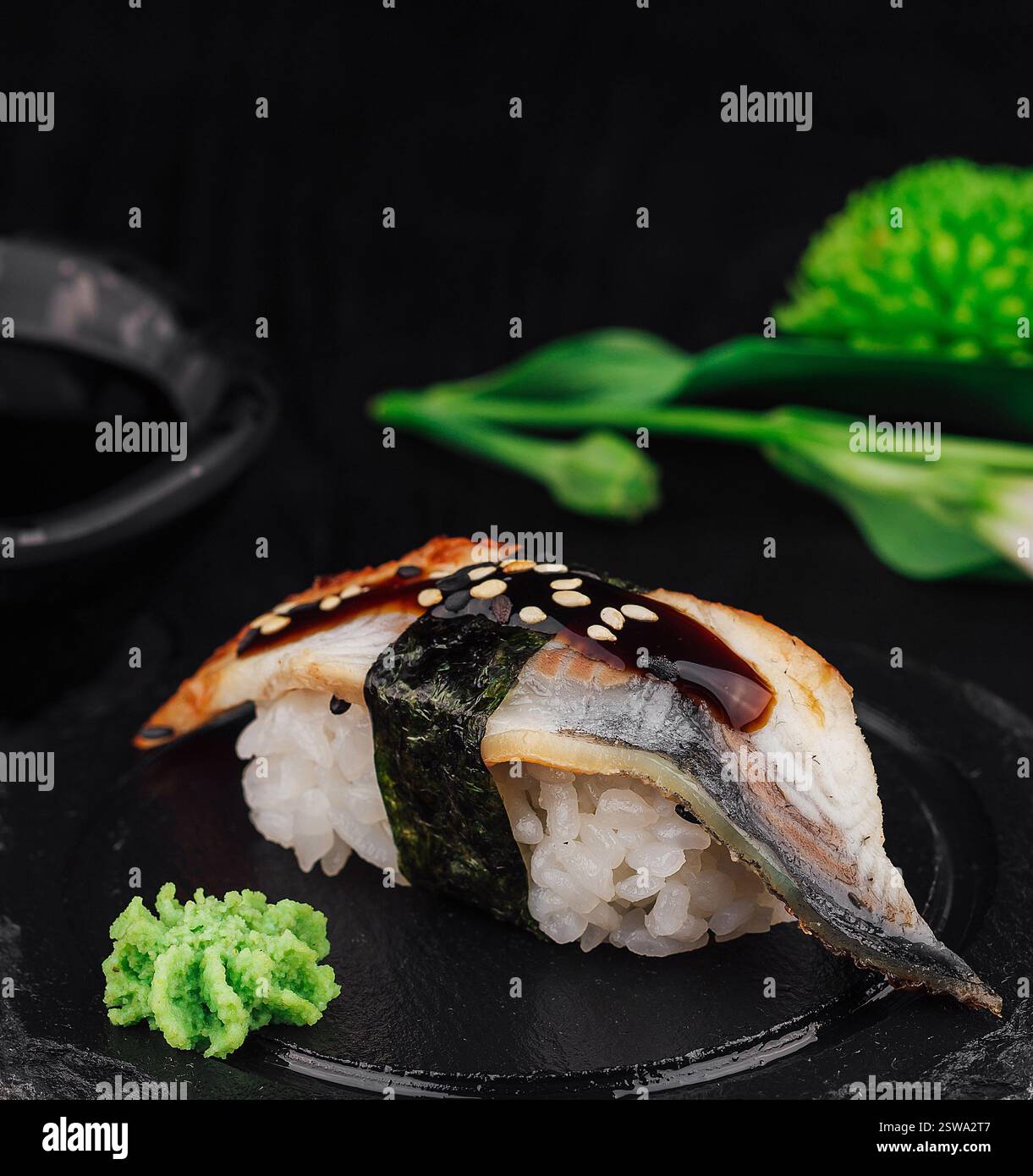 Single unagi nigiri sushi with eel, rice, nori seaweed, sesame seeds and unagi sauce on a black ...