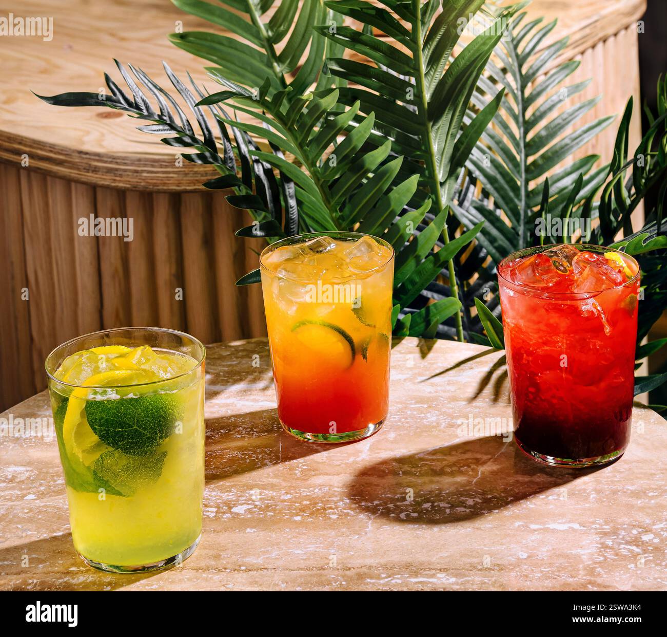 Three colorful cocktails are sitting on a travertine table with ...