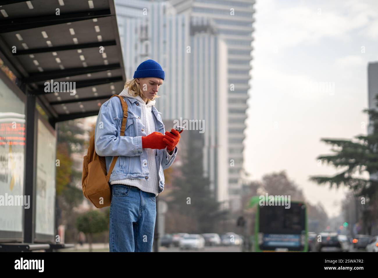 Male student standing at bus stop, looking at route on GPS navigator ...