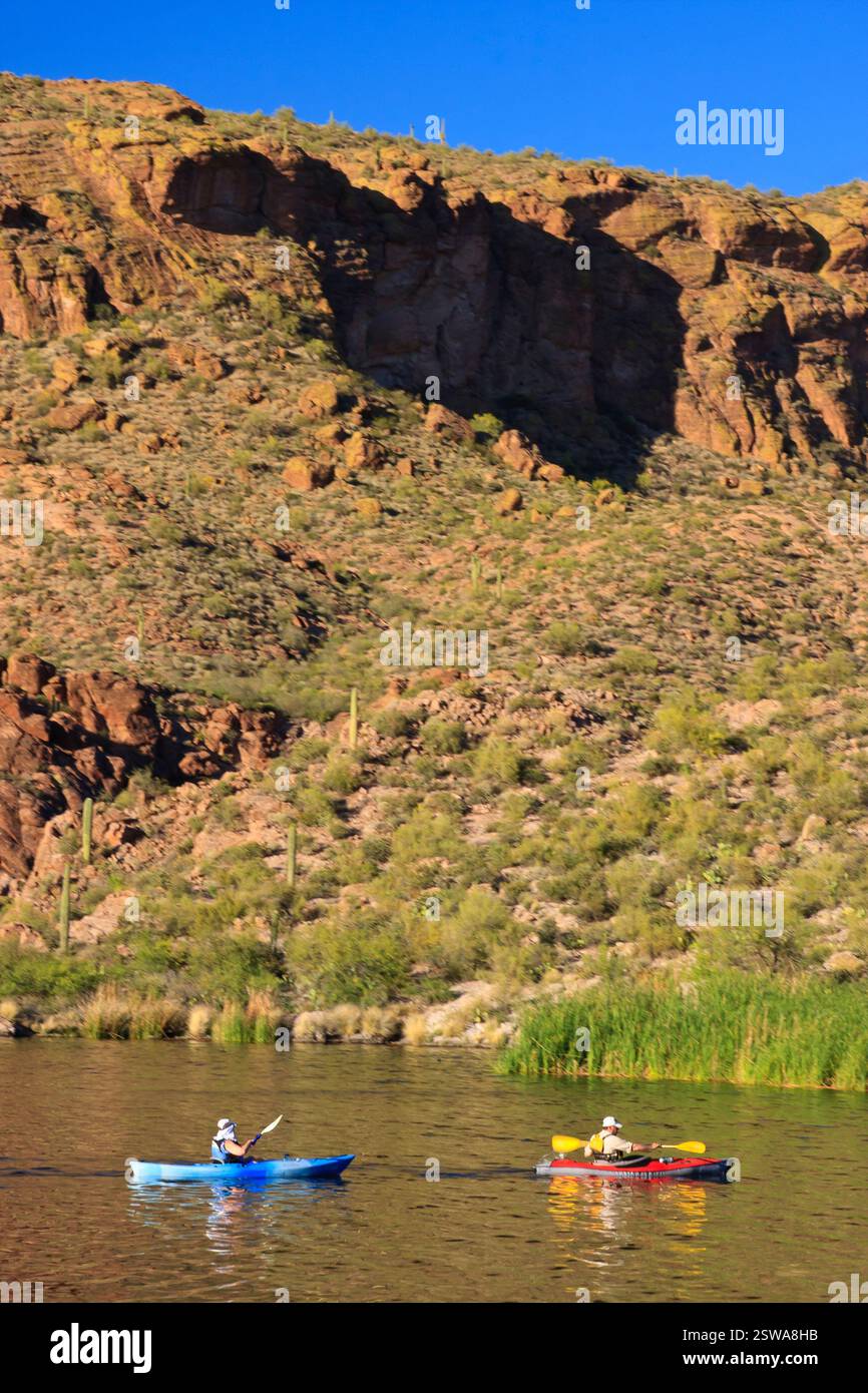 Two people are paddling kayaks on a river. The water is calm and the ...