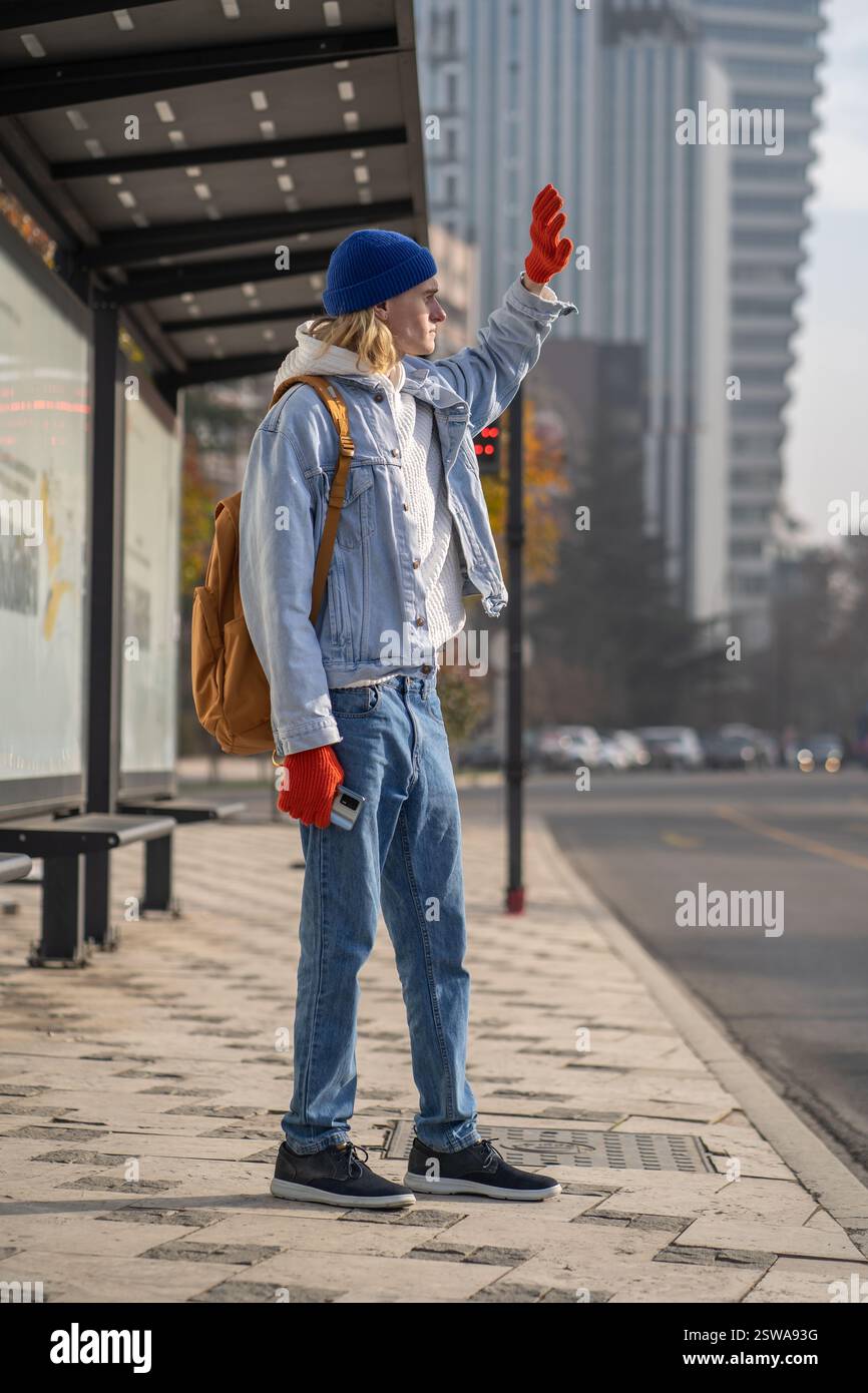 Young guy traveler at bus stop waiting for transport covered with hand ...