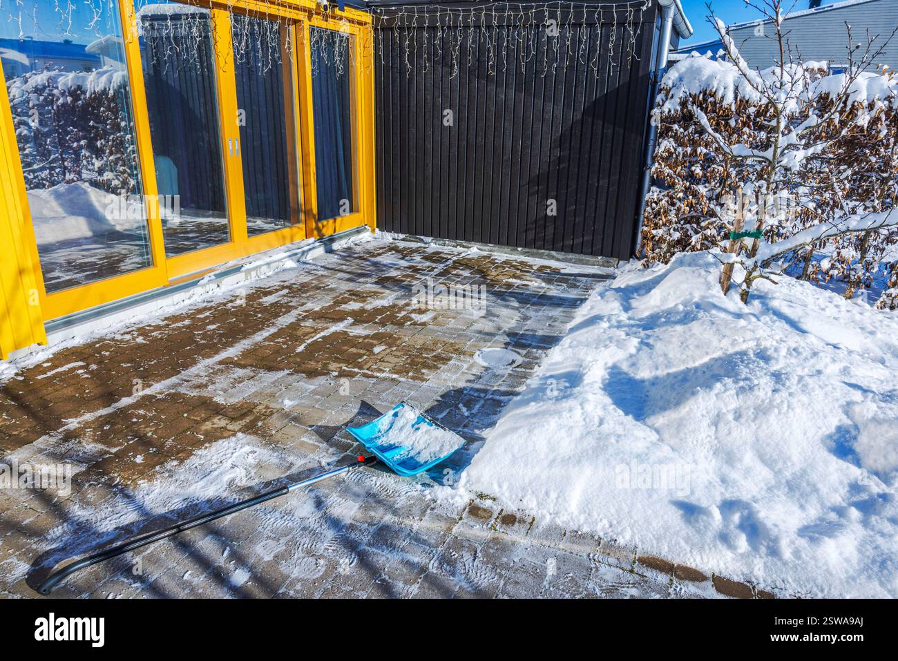 Blue snow shovel lying on cleared brick patio near panoramic windows of ...