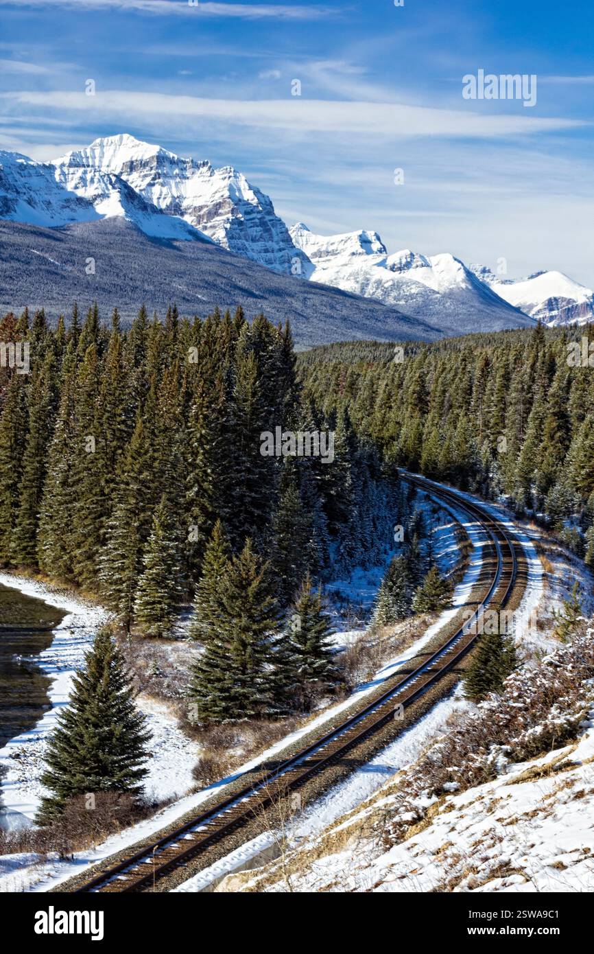 Train tracks run through a snowy forest with mountains in the ...