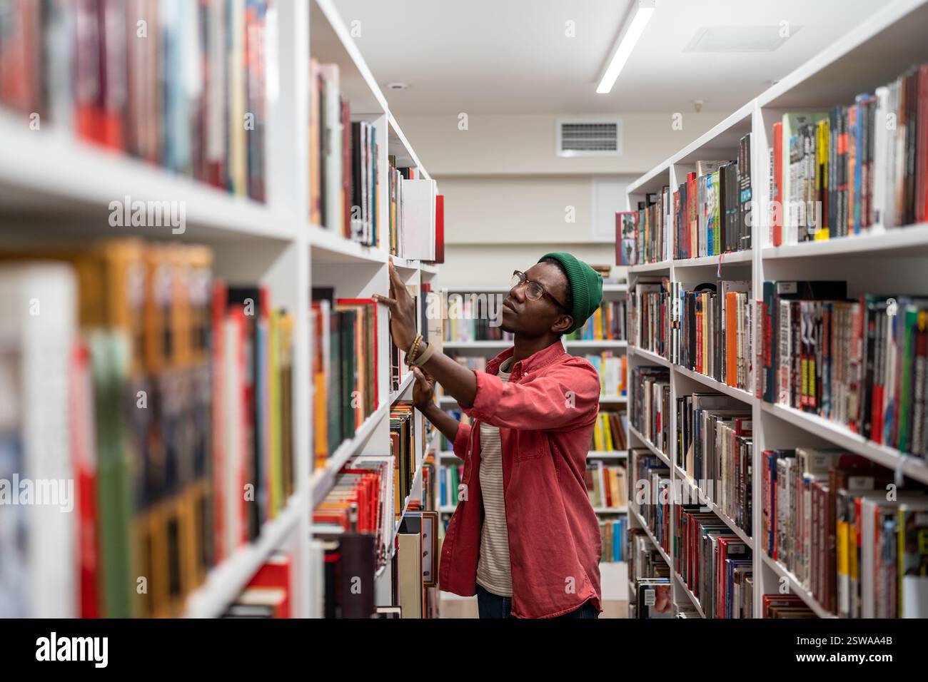 Thoughtful African American student man in glasses choosing book in ...