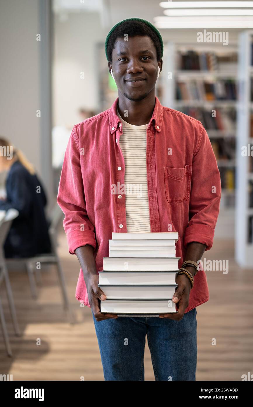 Portrait of happy African American student guy with pile of books in ...