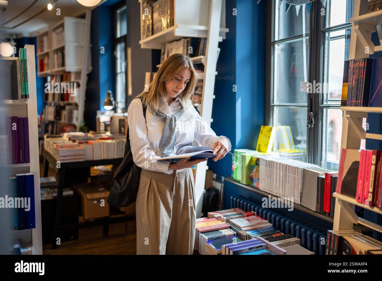 Focused thoughtful middle aged woman reading book standing shopping in ...