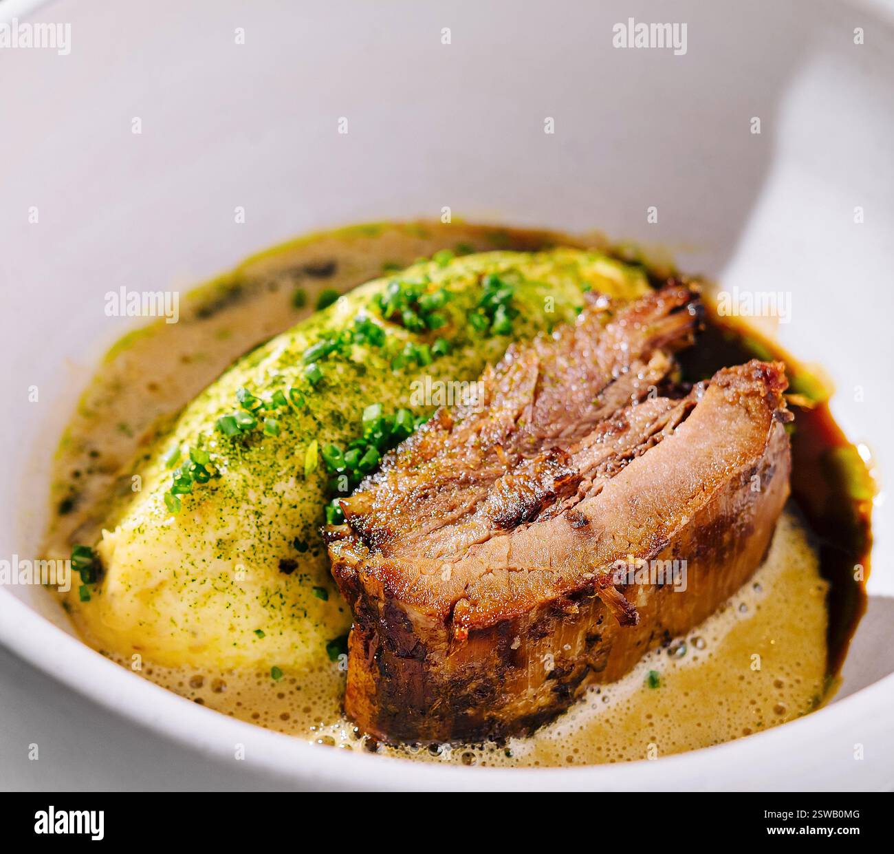 Braised beef short rib with parsnip puree and chives plated in a white ...