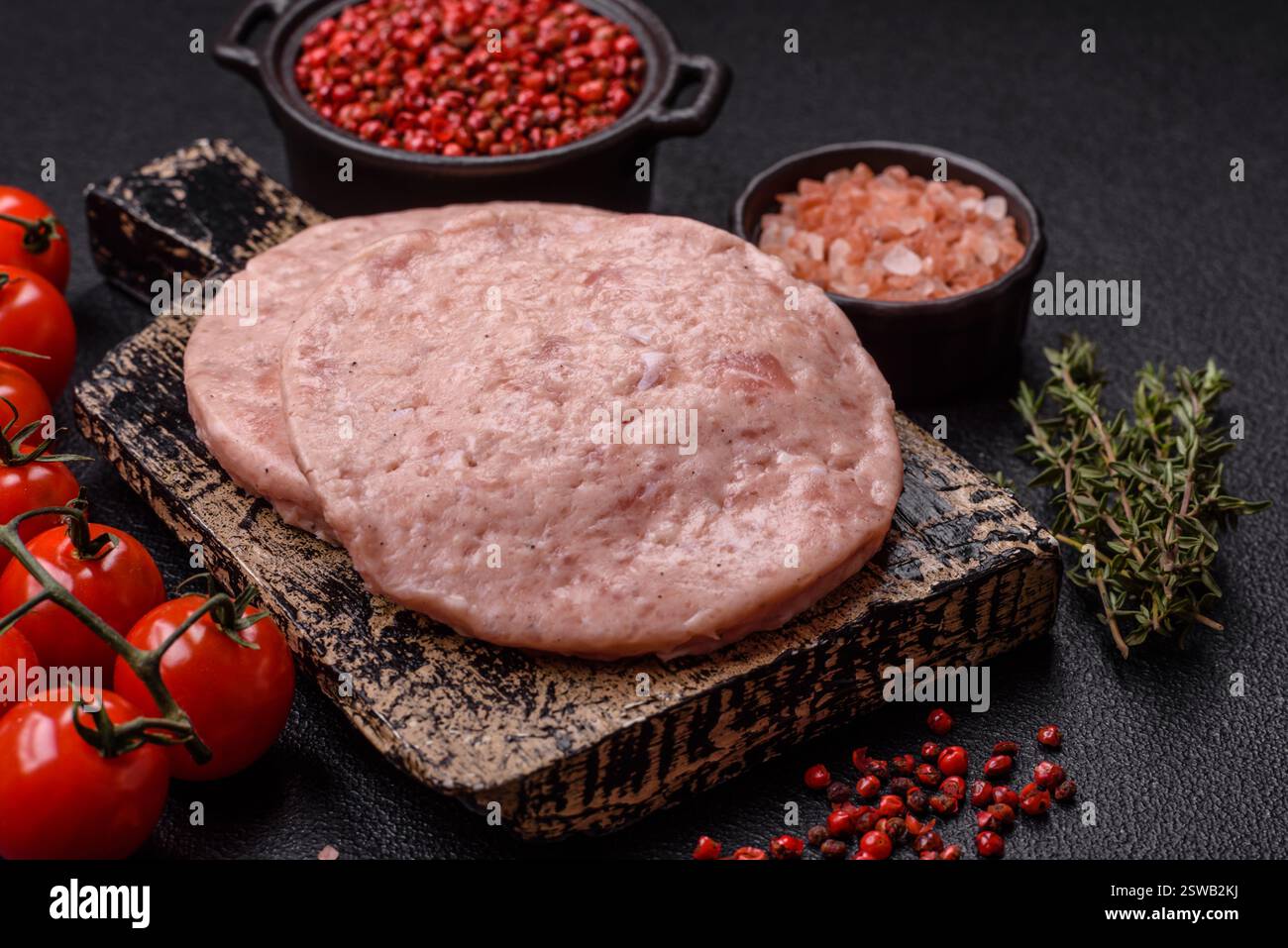 Raw chicken burger cutlet with salt, spices and herbs on dark concrete ...
