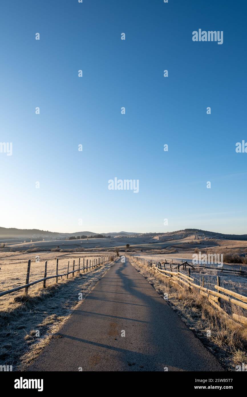 A paved road winds through a frosty rural landscape under a clear blue ...