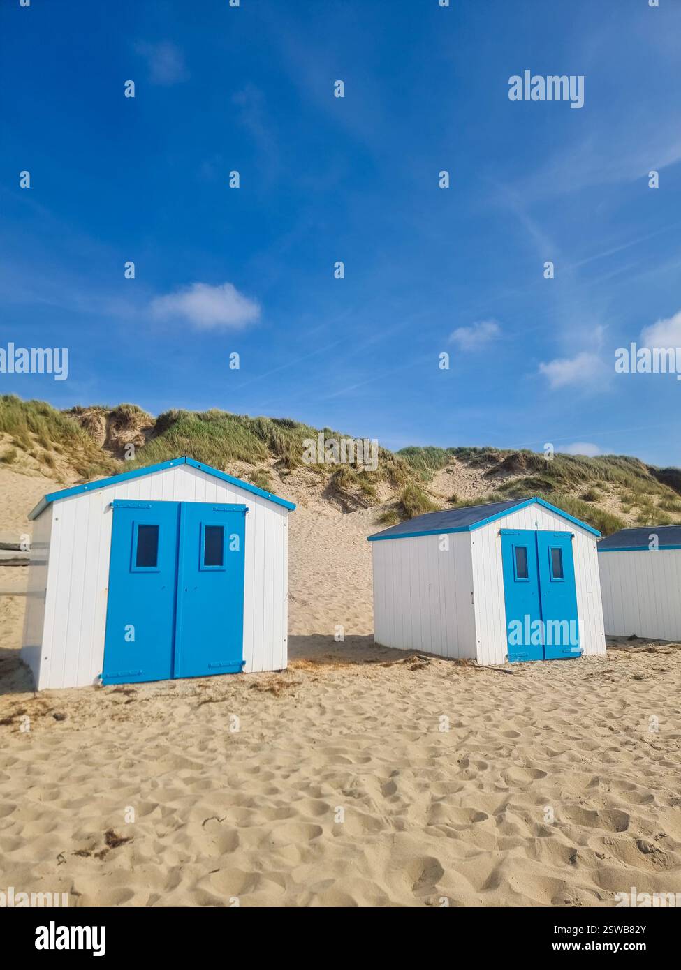 Bright blue beach huts stand against a sandy landscape under a clear ...