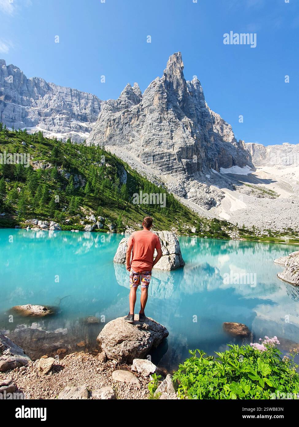 A solitary figure stands on a rock, gazing over a serene turquoise lake ...
