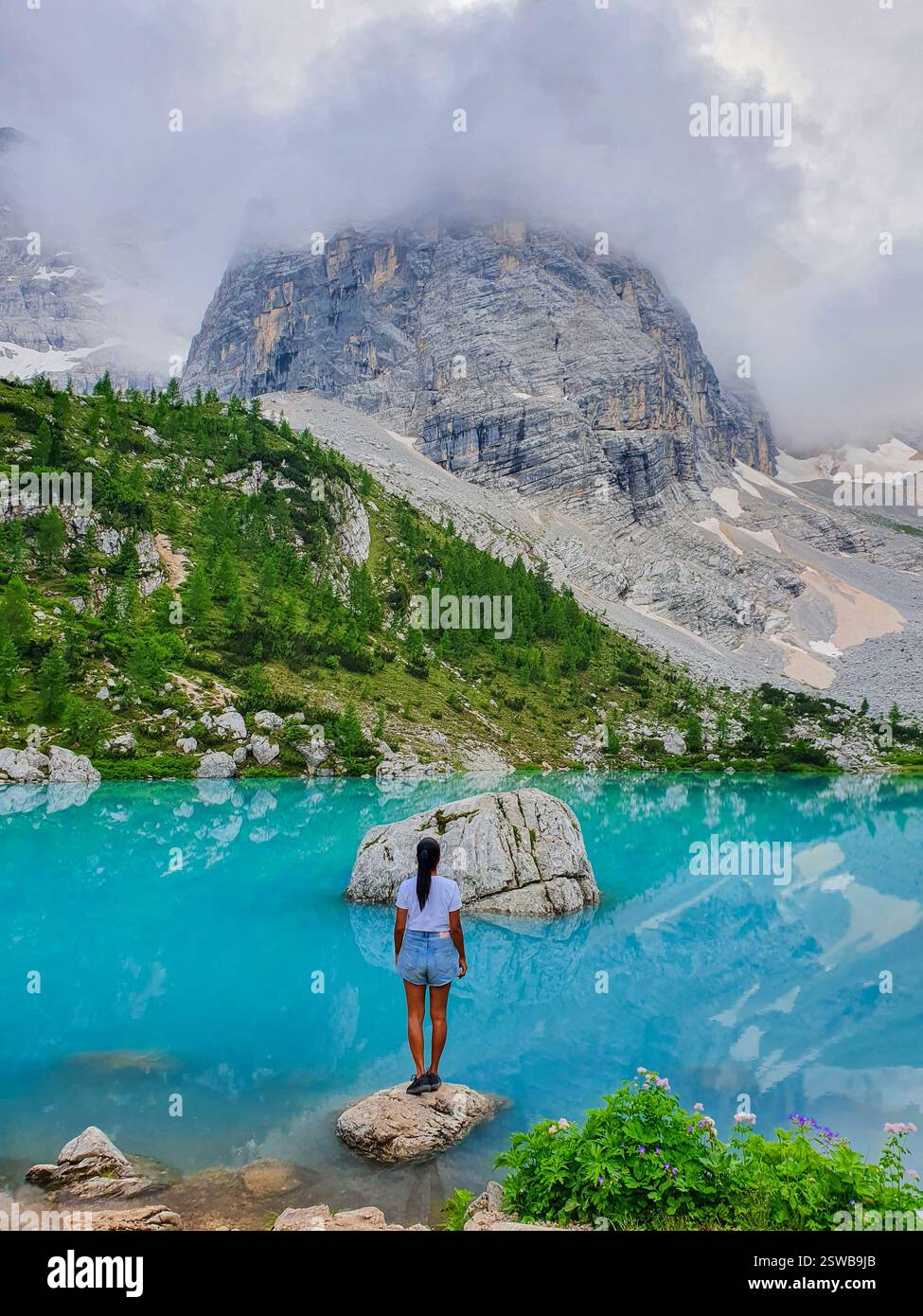 A person stands on a rock, gazing at a stunning turquoise lake ...