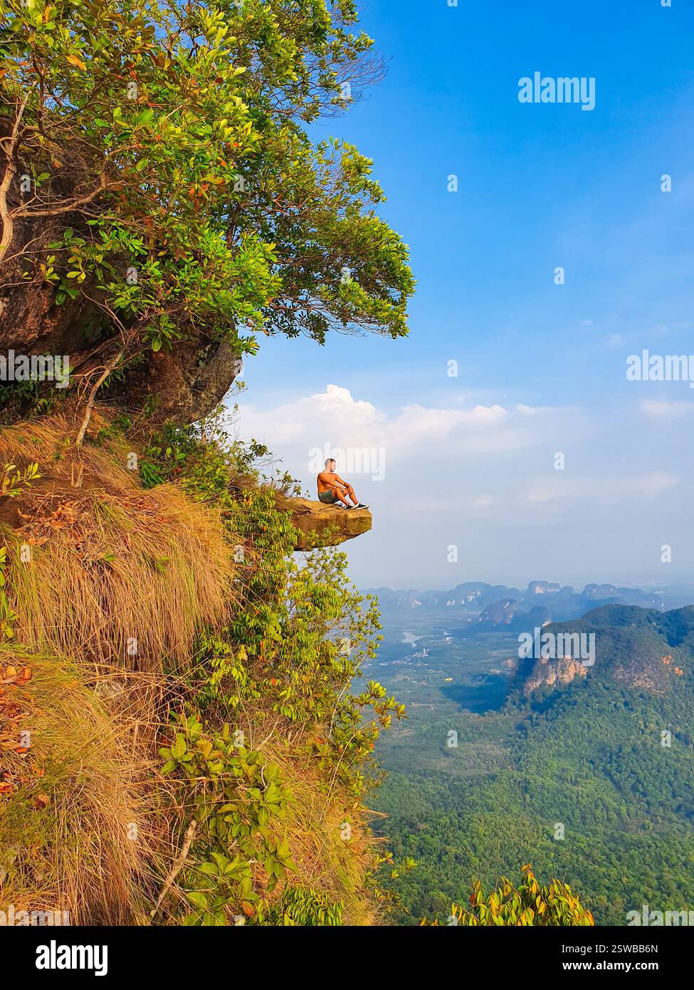 High above a lush valley, a lone figure sits peacefully on a rocky ...
