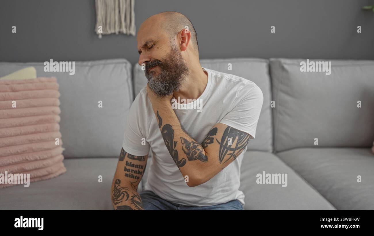 Handsome man with a beard and tattoos feeling neck pain in a modern ...