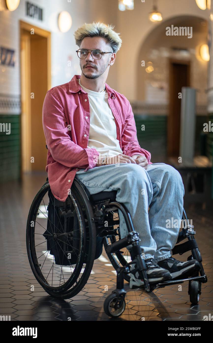 Man with disability in wheelchair in public hall, thoughtfully looking ...