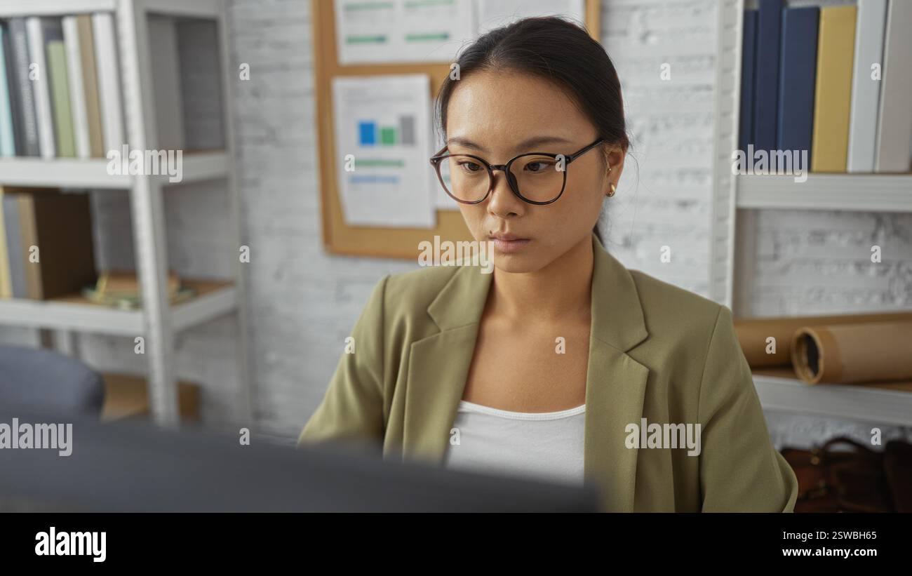 Young chinese woman working at an office desk with focus, wearing ...