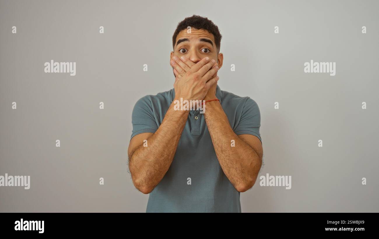 Young hispanic man covering mouth with hands while standing isolated over white background Stock ...