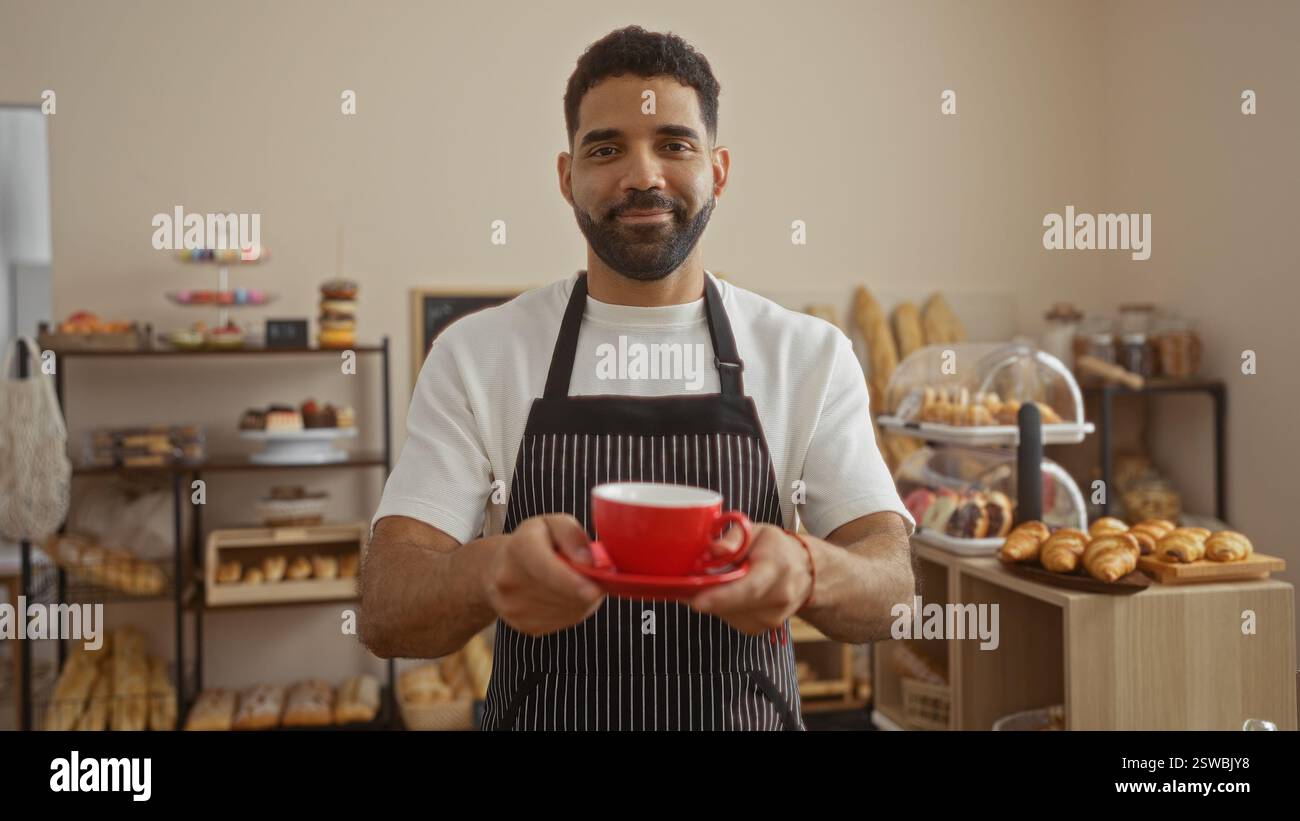 Handsome man in a bakery holding a red cup, surrounded by baked goods ...