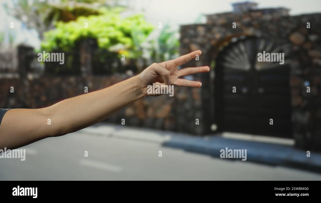 Man's hand showing three fingers in an outdoor city street setting ...