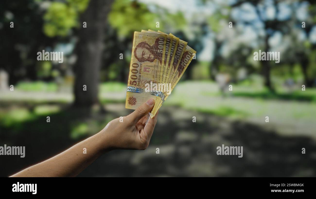 Hand holding hungarian forint banknotes outdoors in a park setting ...