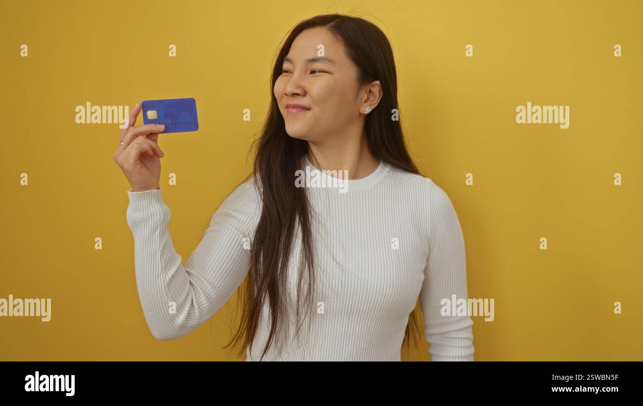 Woman smiling holding a credit card over a bright yellow background ...