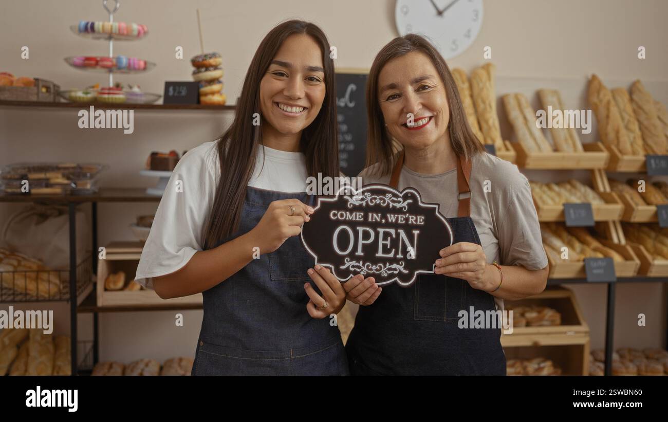 Two smiling women wearing aprons holding an 'open' sign inside a cozy ...