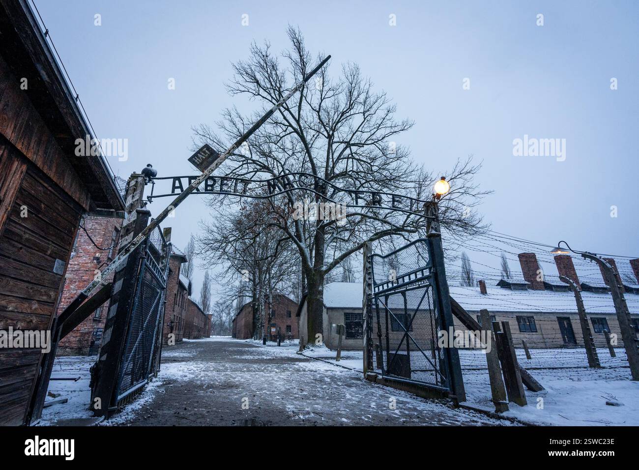 Entrance gate of Auschwitz on a snowy evening with streetlights glowing ...