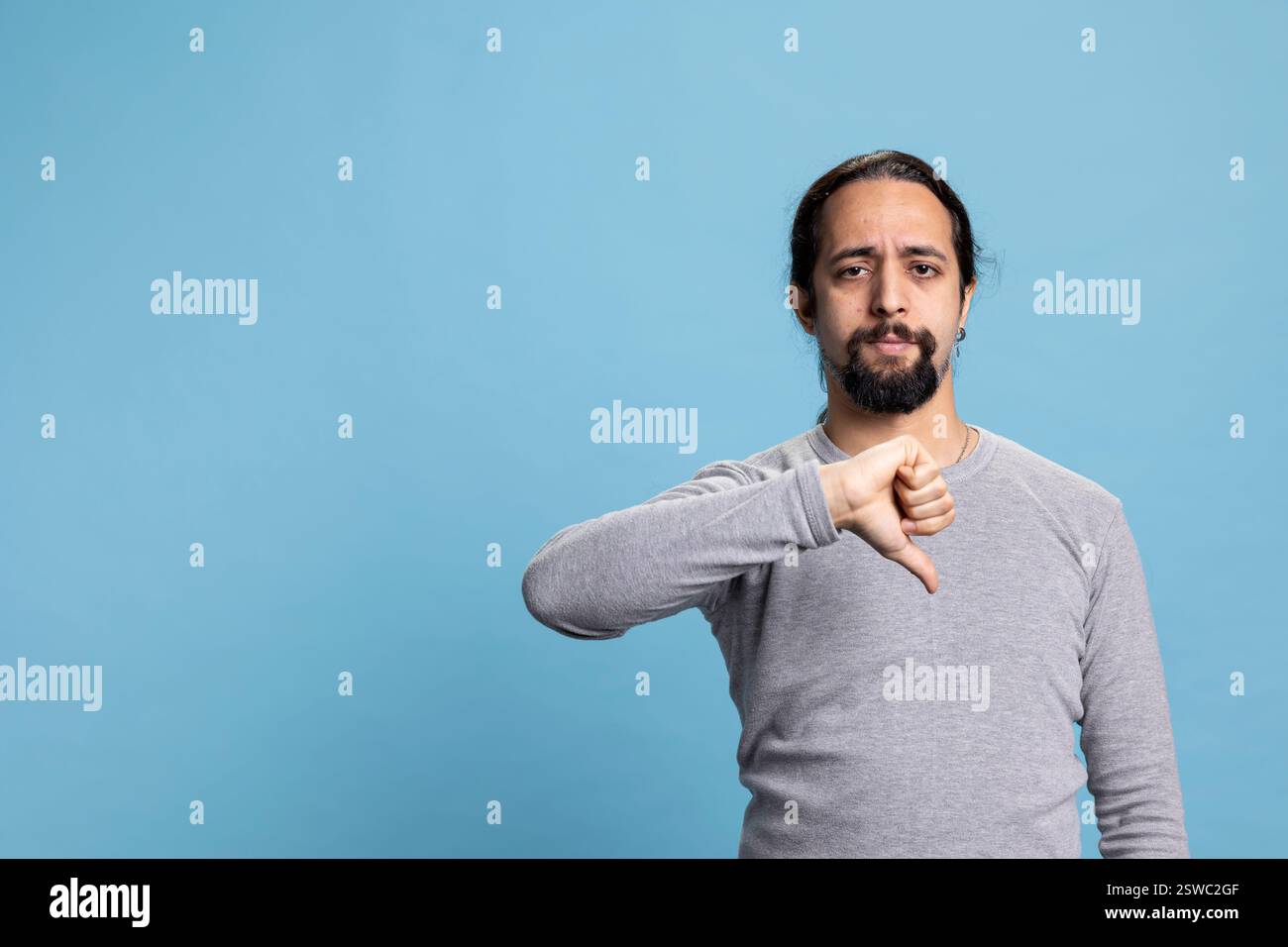 Young dissatisfied person showing thumbs down symbol in studio ...