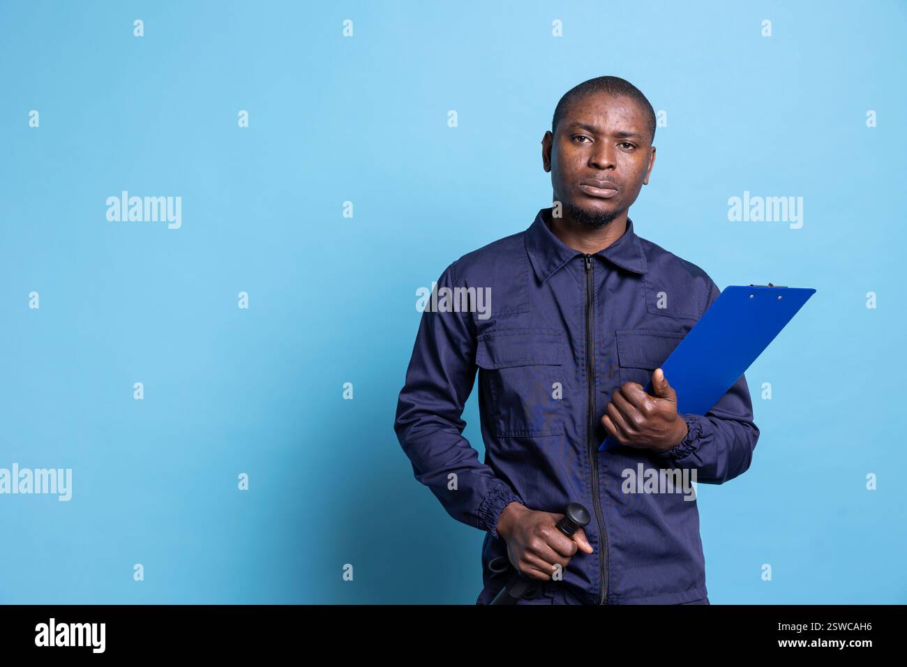 Serious security guard holding his baton weapon and papers in studio ...