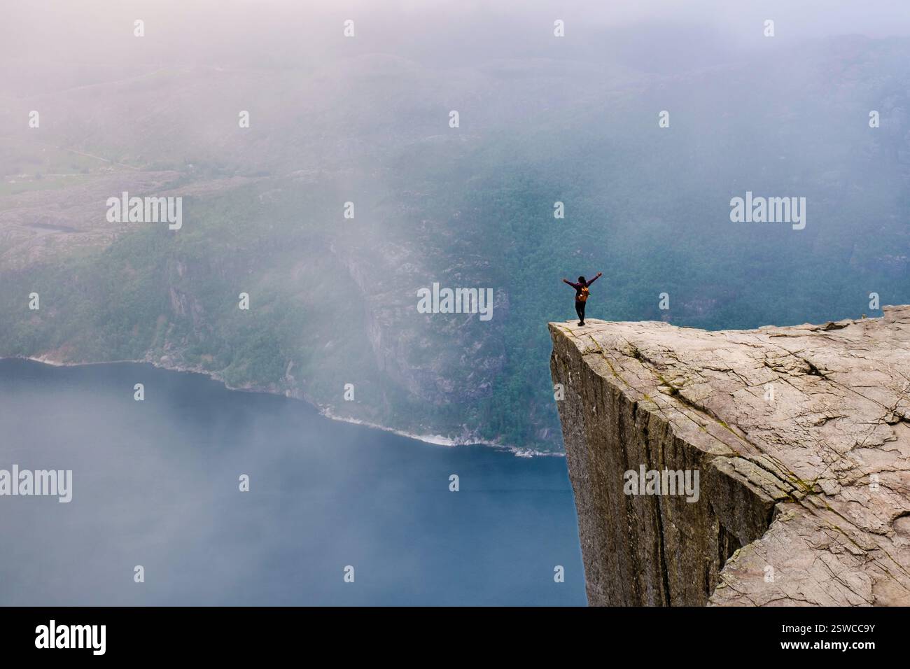 Preikestolen, Norway, A hiker stands on the edge of a cliff with arms ...