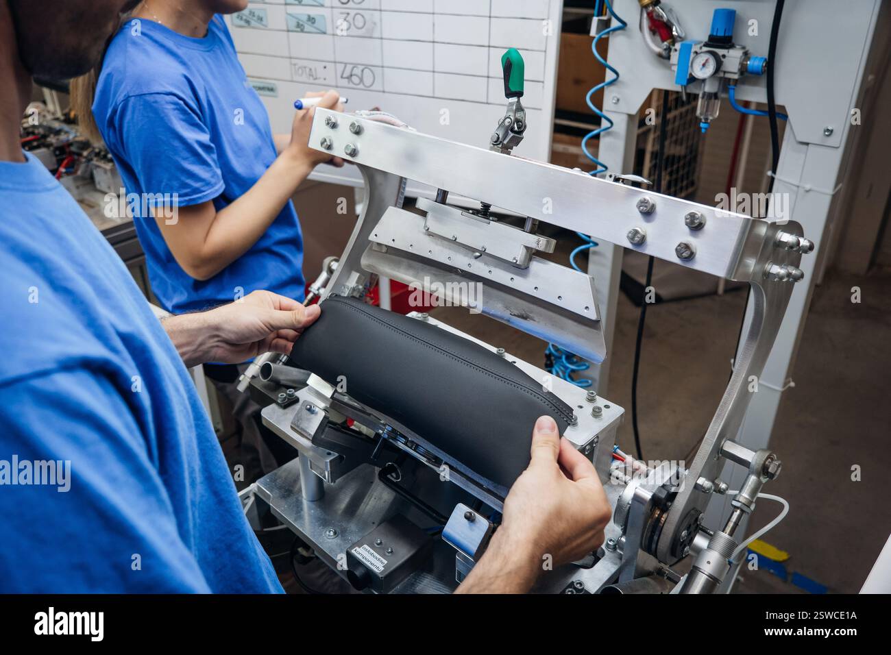 Manufacturing workers align a black component within a machine for a precise fit ensuring ...