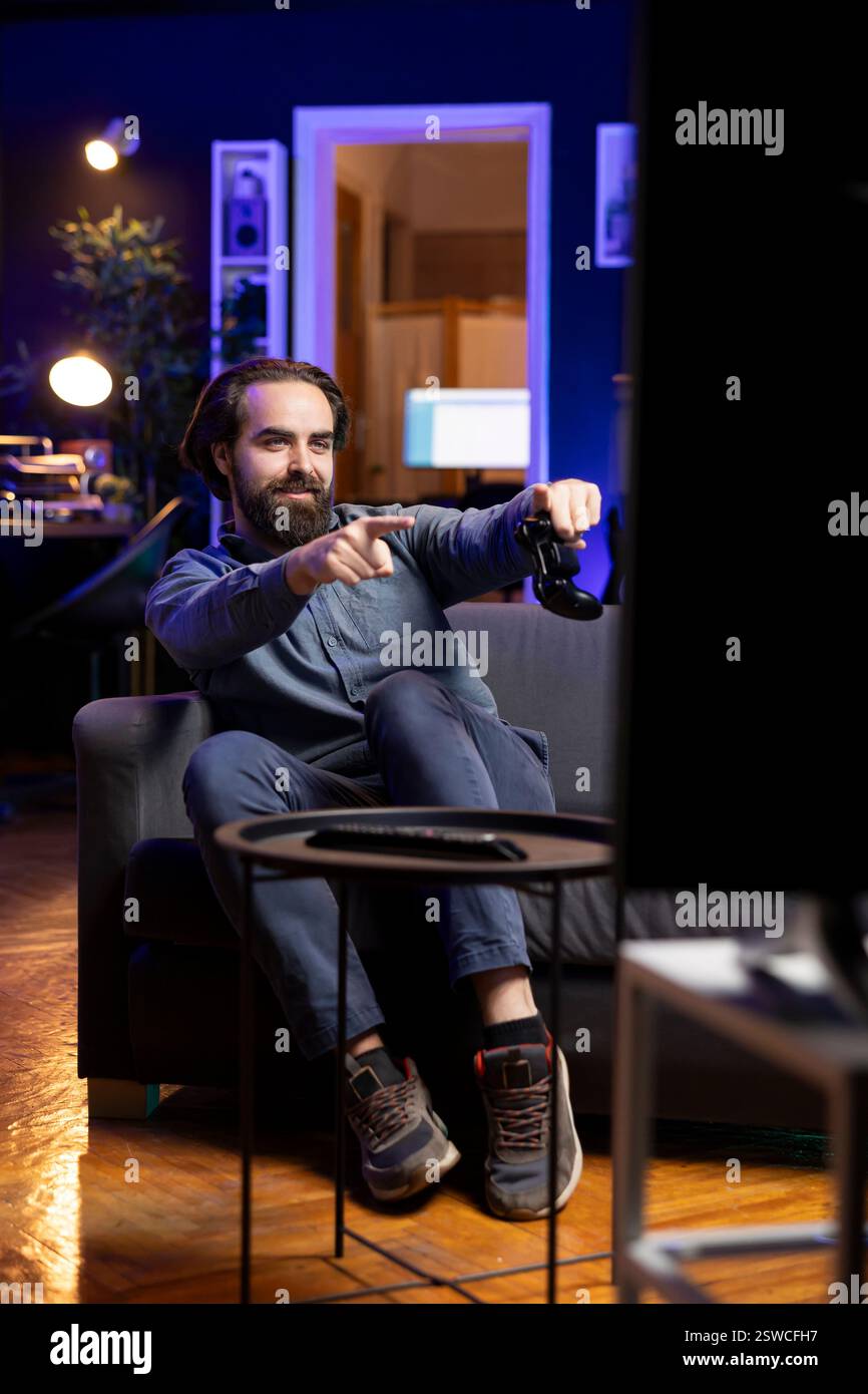 Smiling man pointing to TV while playing videogame in RGB illuminated ...