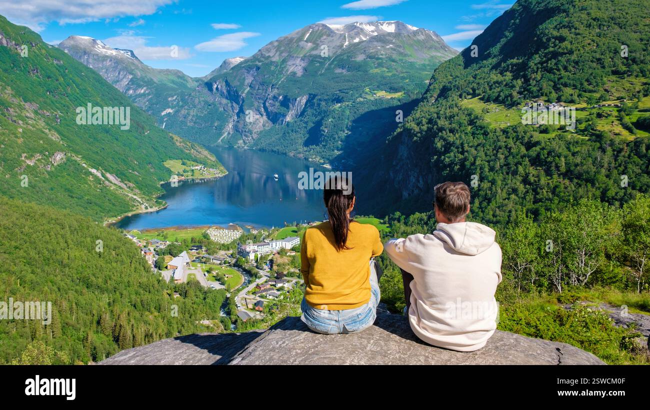 Two people sit on a rocky ledge overlooking a stunning Norwegian fjord ...