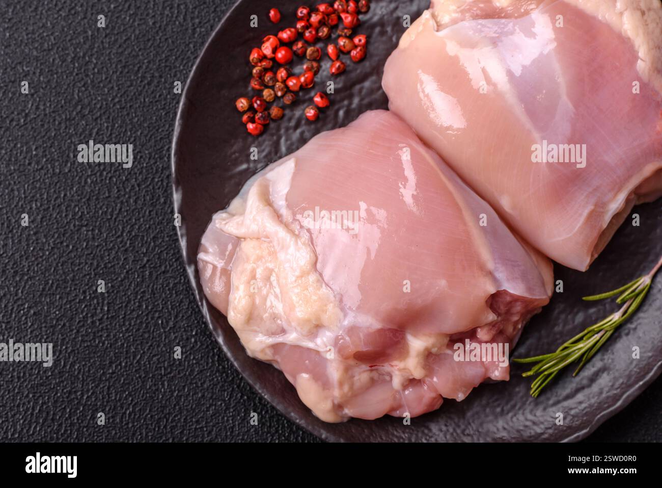 Fresh raw chicken thigh fillets with salt, spices and herbs on a dark ...