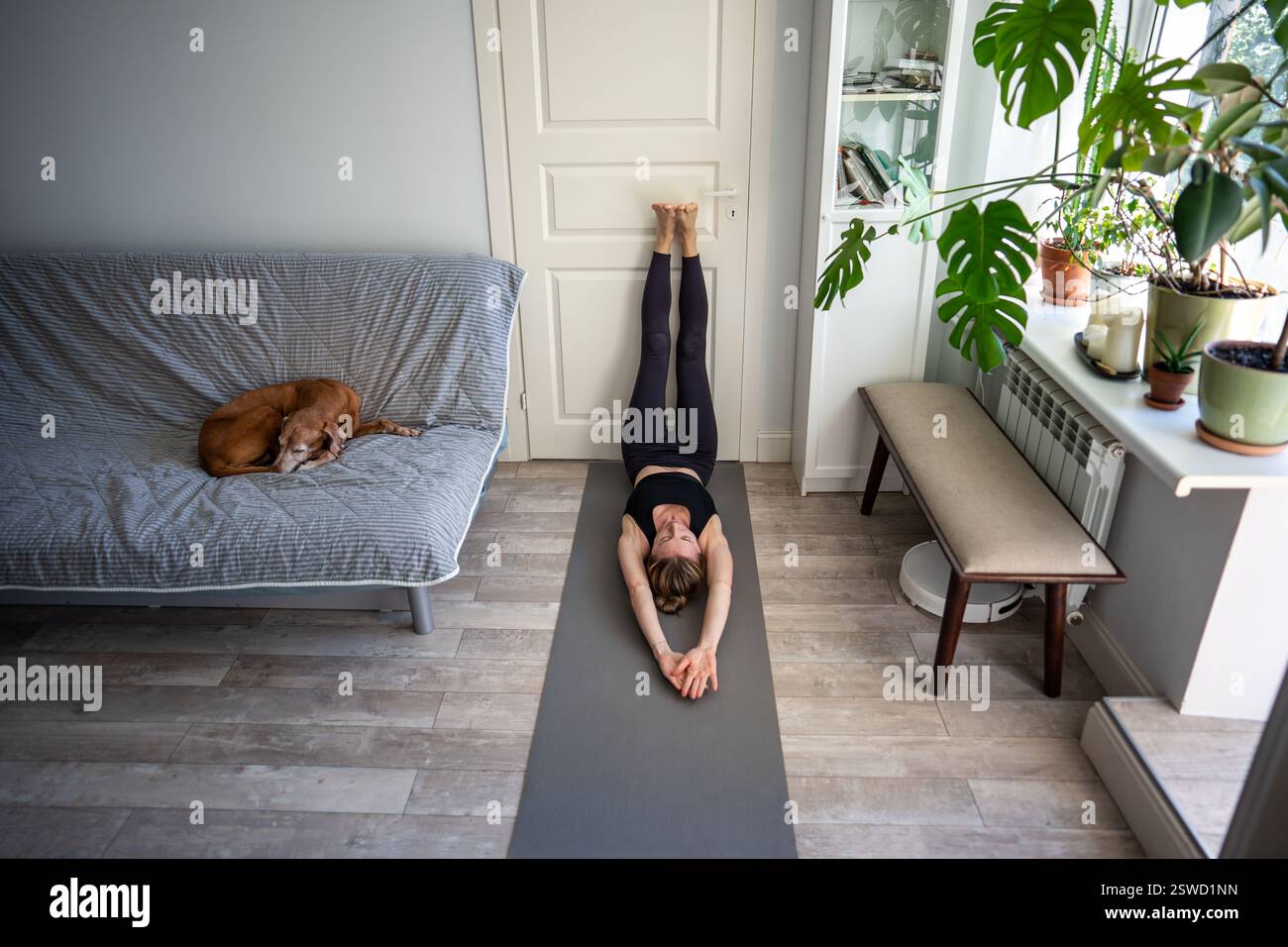 Spiritual woman lies on yoga mat with feet against door, arms stretched ...
