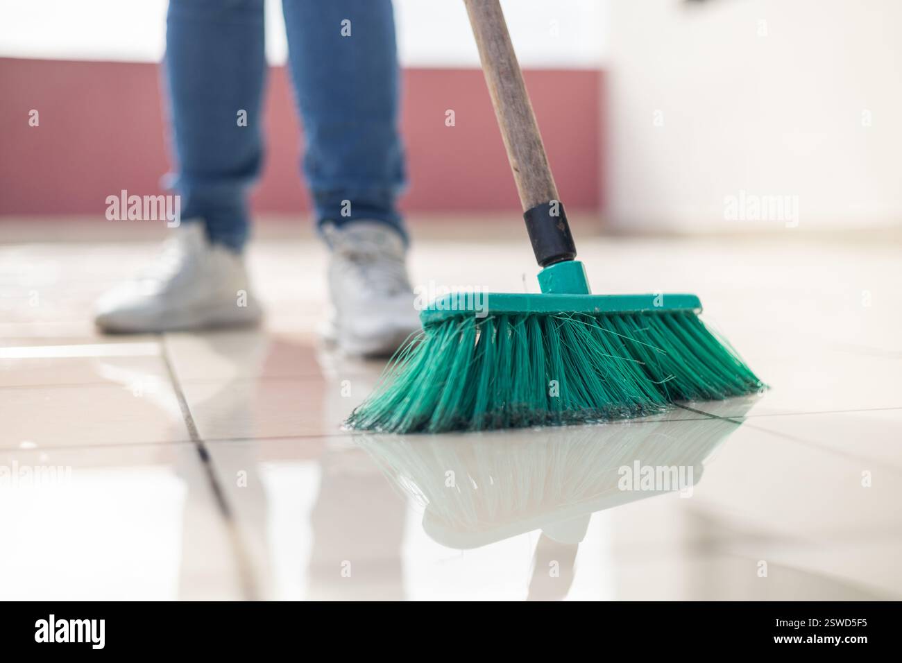 A woman sweeping the floor, showing her legs and shoes, wearing jeans ...