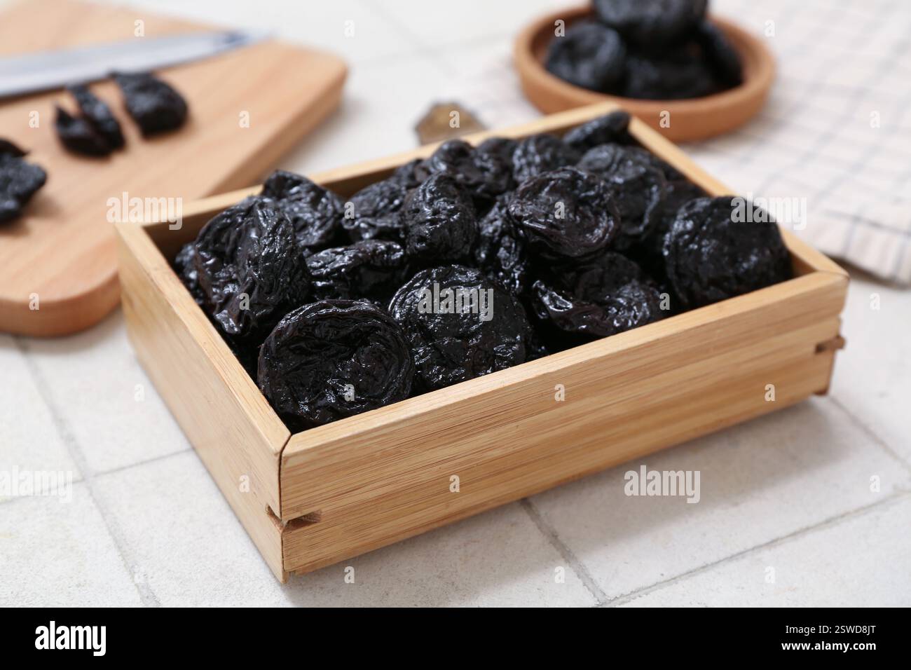 Wooden box with dried prunes on white tile background Stock Photo - Alamy