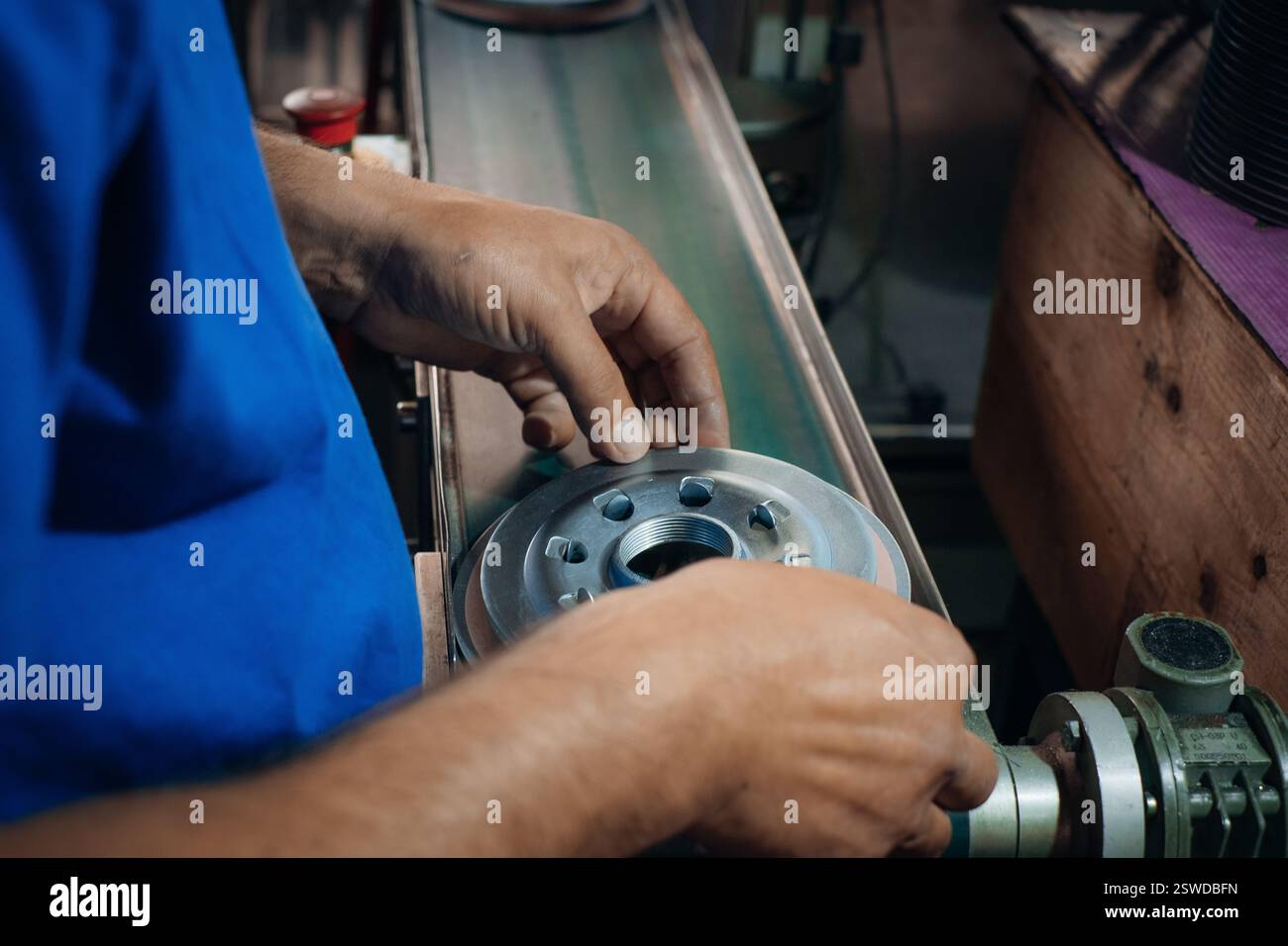 A worker places a metal part on a moving conveyor belt ensuring quality ...