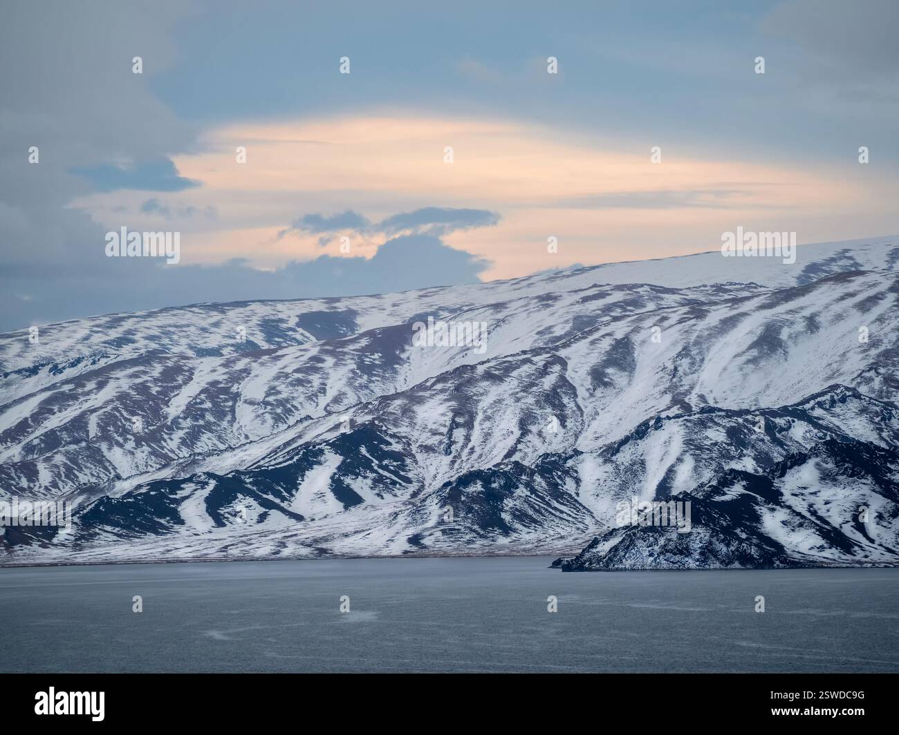 Pastel colors with the snow covered mountains and dark lake in the ...