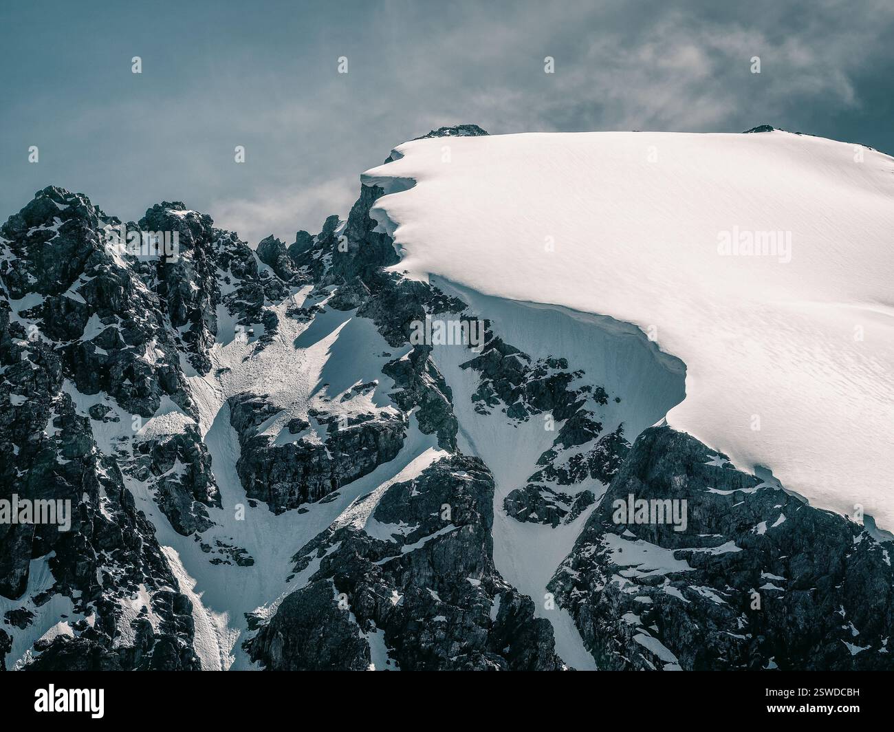 Bright alpine landscape with snow-covered mountain top and black rocks ...