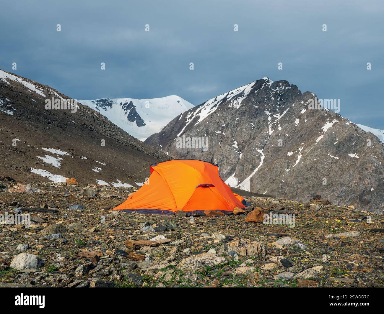 Orange tent on a sunny mountain slope. Camping on a rocky high-altitude ...