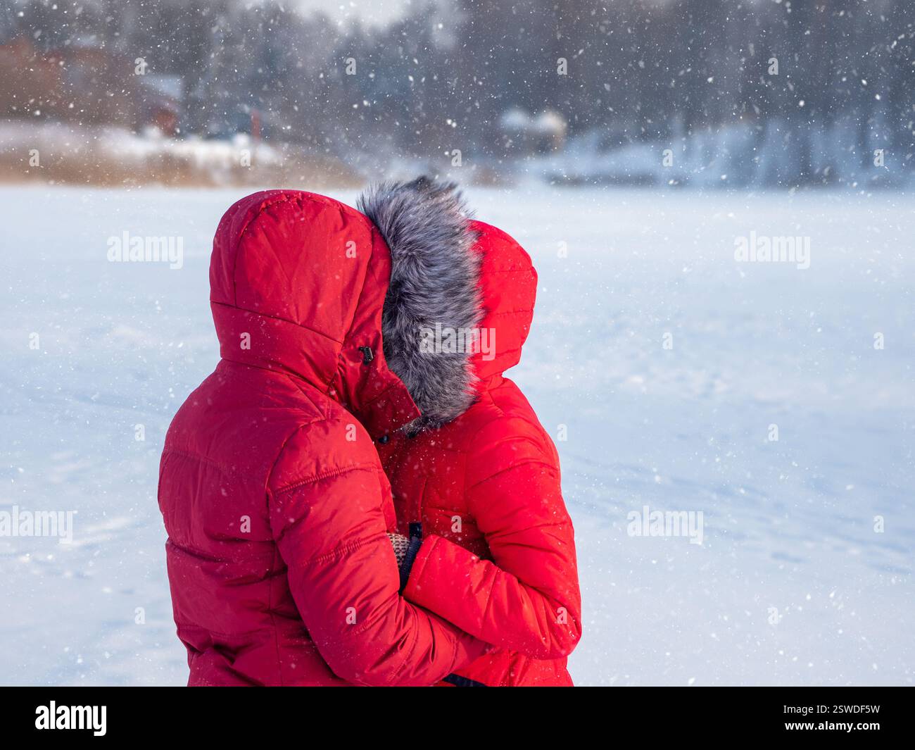 Love in the cold. A couple in red jackets hugging in the snow in winter ...