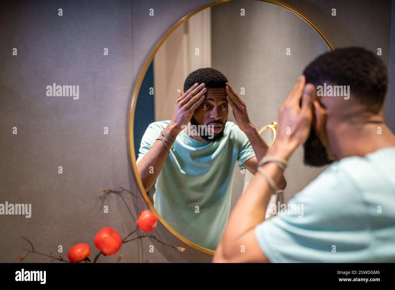 Unhappy African American 30s man touching face skin looking at mirror ...