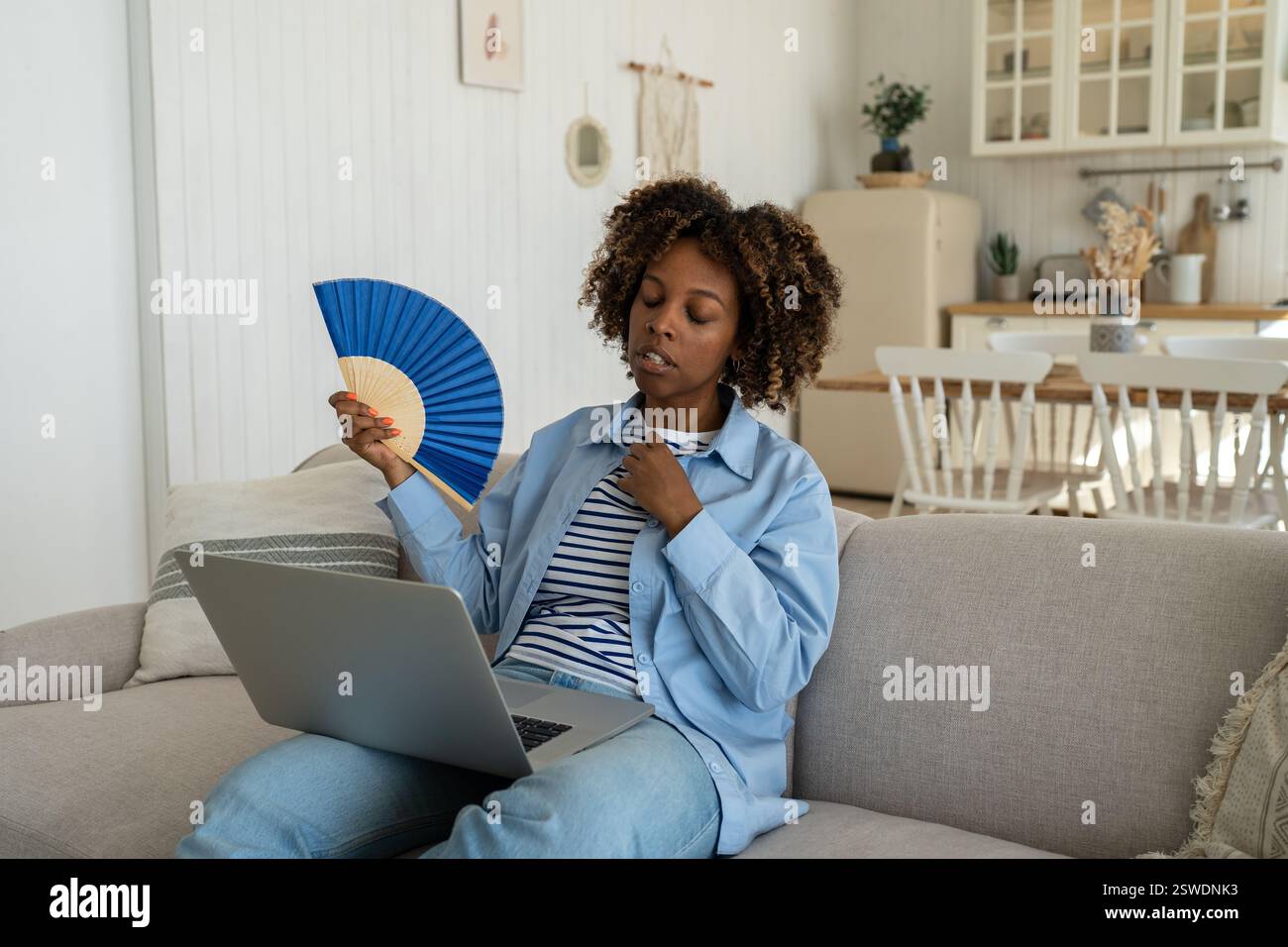 Tired african woman waving fan in hand suffer from heat day while work ...
