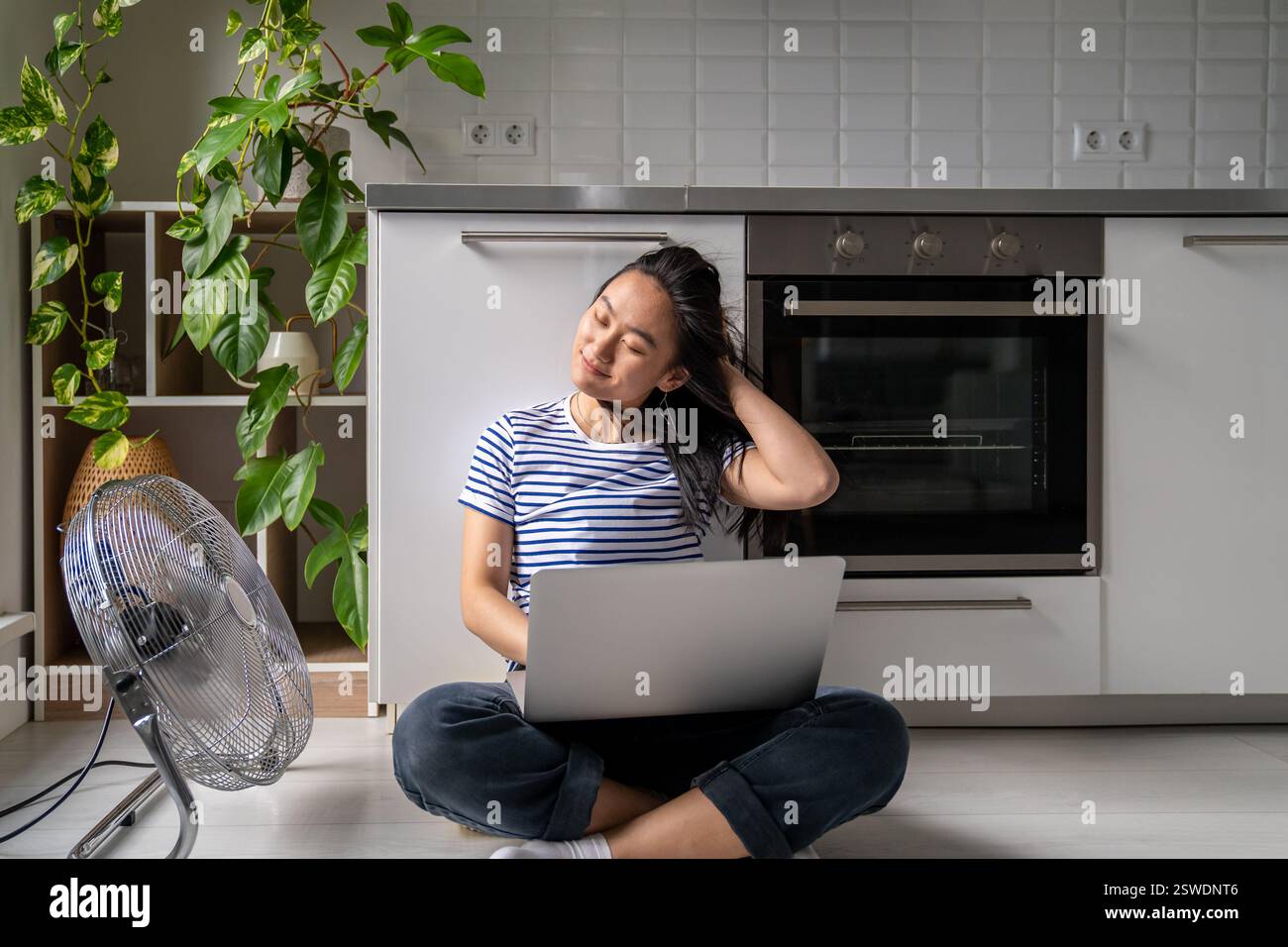 Contented Asian woman turn on floor ventilator fan while work with ...