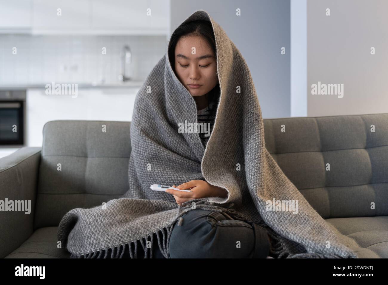 Sad Asian girl trying to warm feel cold ill sick suffering from fever ...