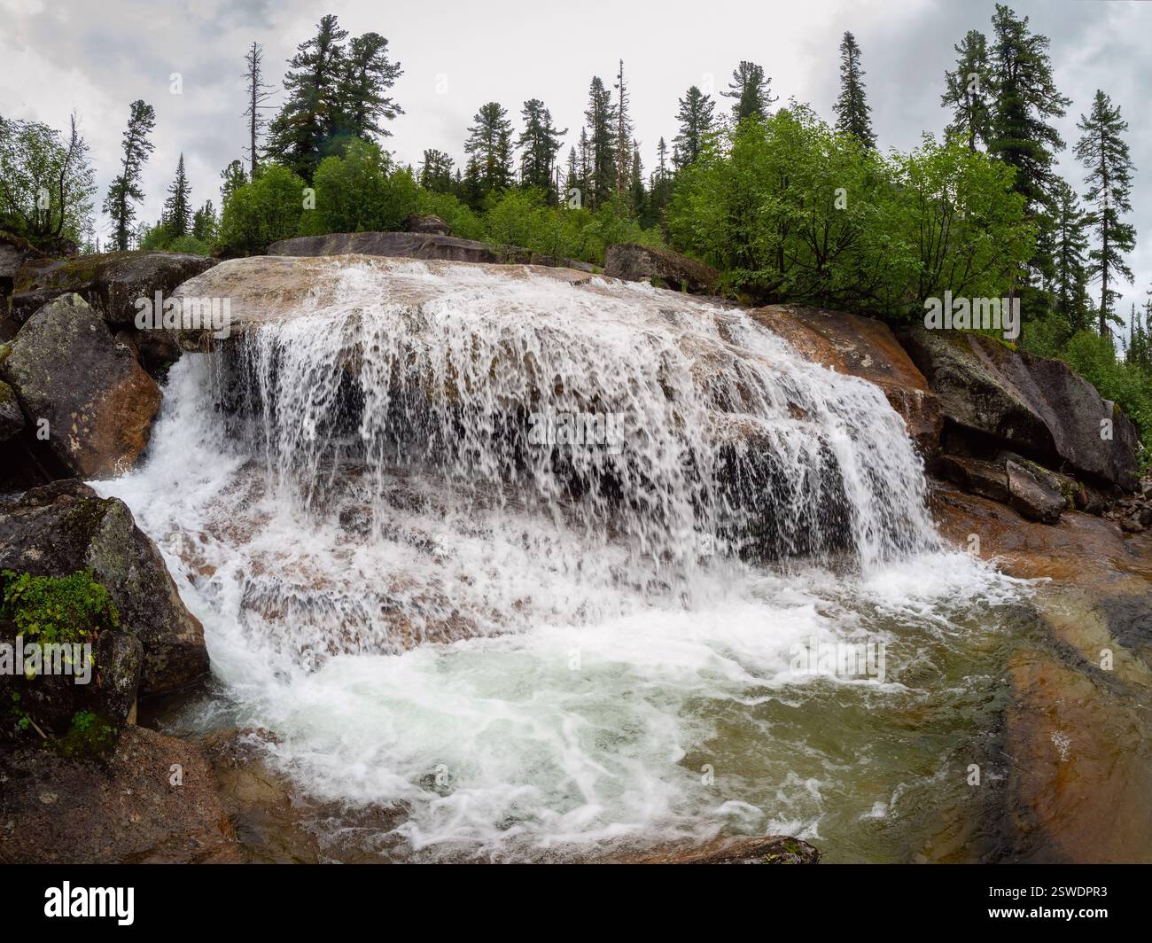 Cascades of a powerful waterfall in a green mountain forest. Nature ...