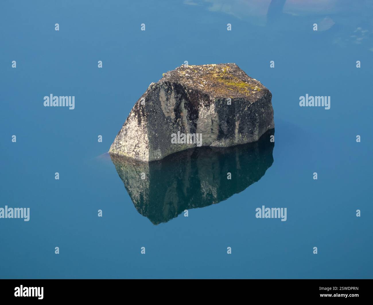 Huge boulder in the lake, stone reflection in still clear blue water ...