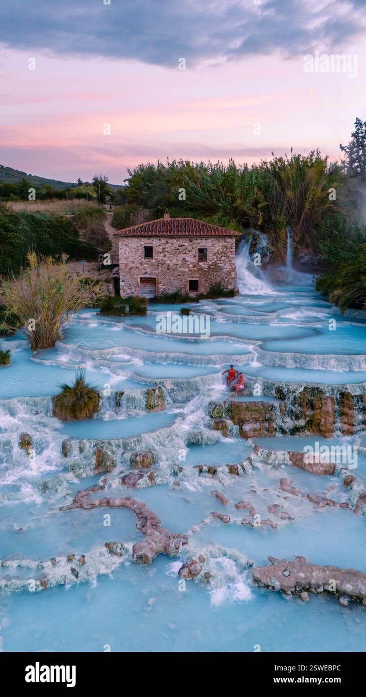 Visitors unwind in the warm, mineral-rich waters of Saturnia thermal baths as waterfalls cascade ...