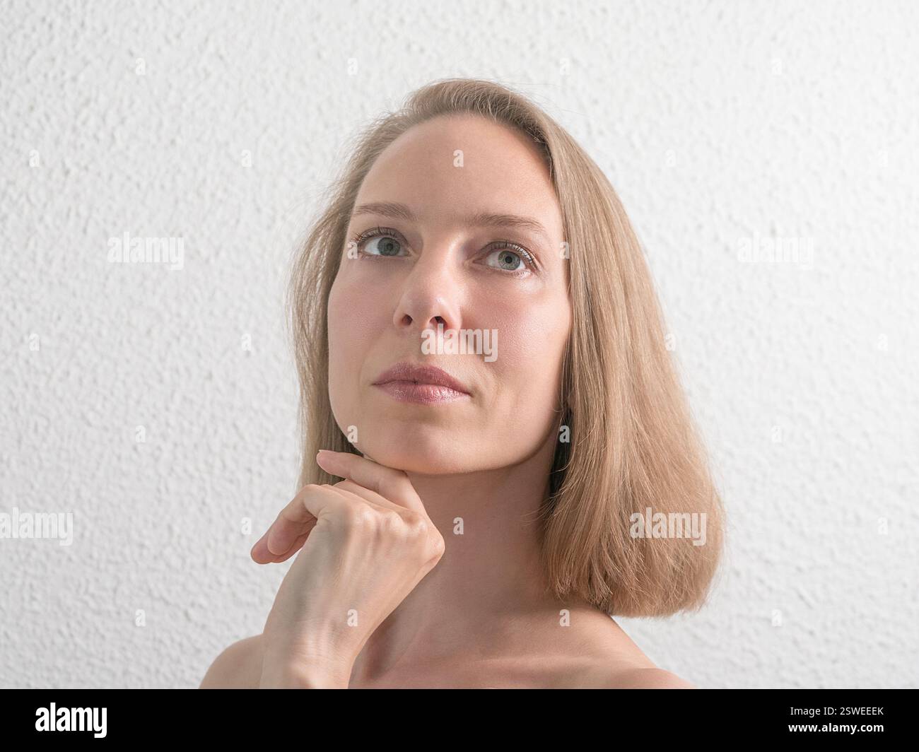 Portrait of beautiful middle aged woman touching her face on white wall. Beauty and skincare ...